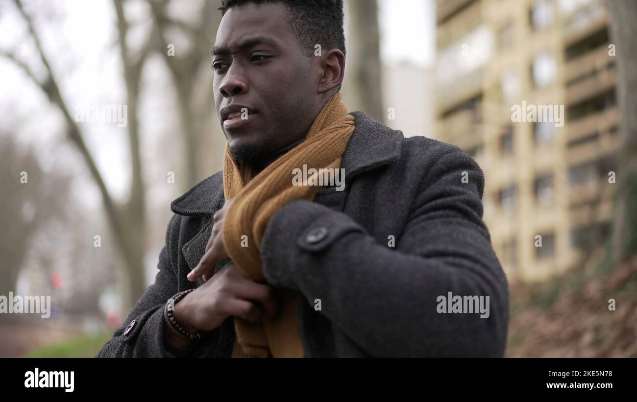 Black man putting scarf outdoors in winter season. African guy ...