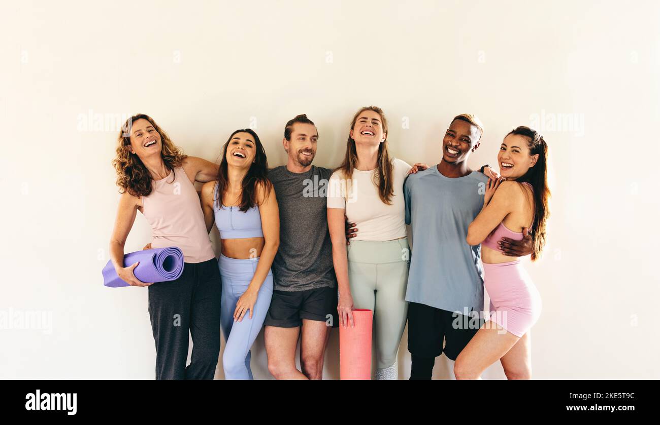 Group of happy fitness friends laughing while standing against a wall ...