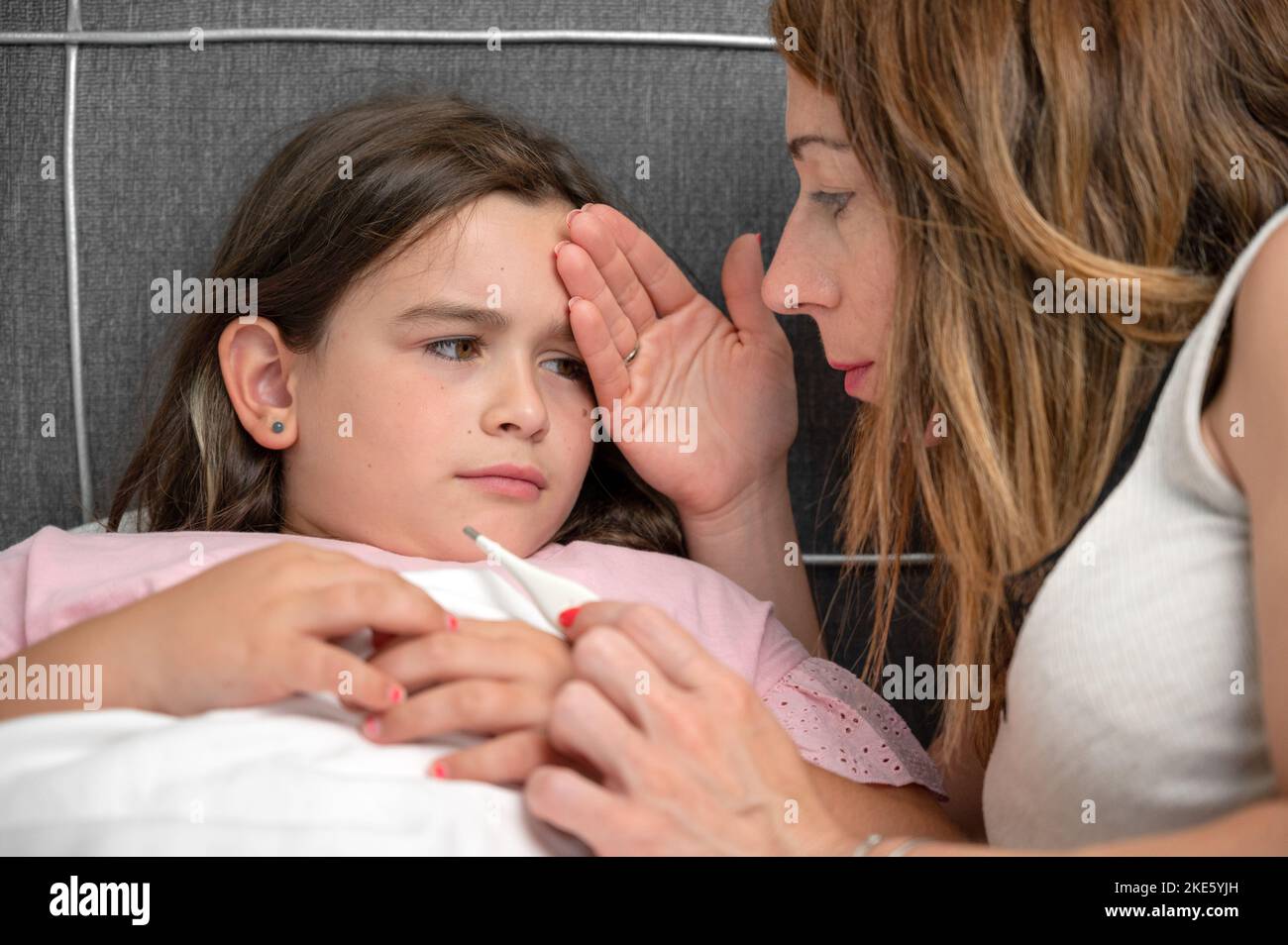 Mother measuring temperature of her ill daughter. Sick child with high fever laying in bed and ...