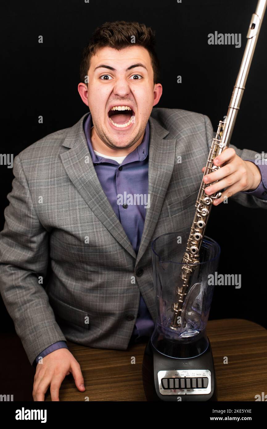 A vertical shot of a guy putting a flute in a blender against a black ...