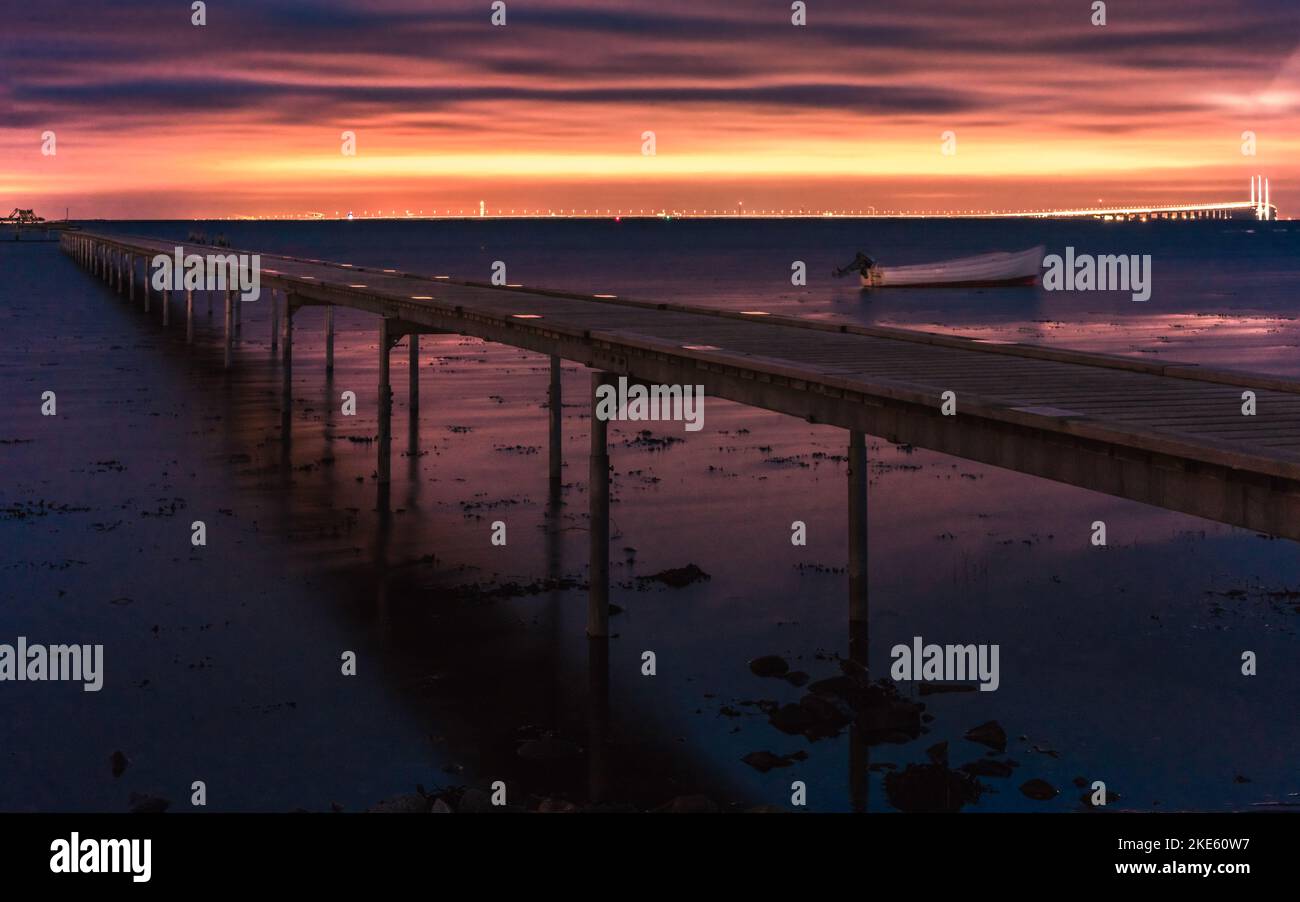 A mesmerizing shot of a sea pier and the colorful sunset giving a ...