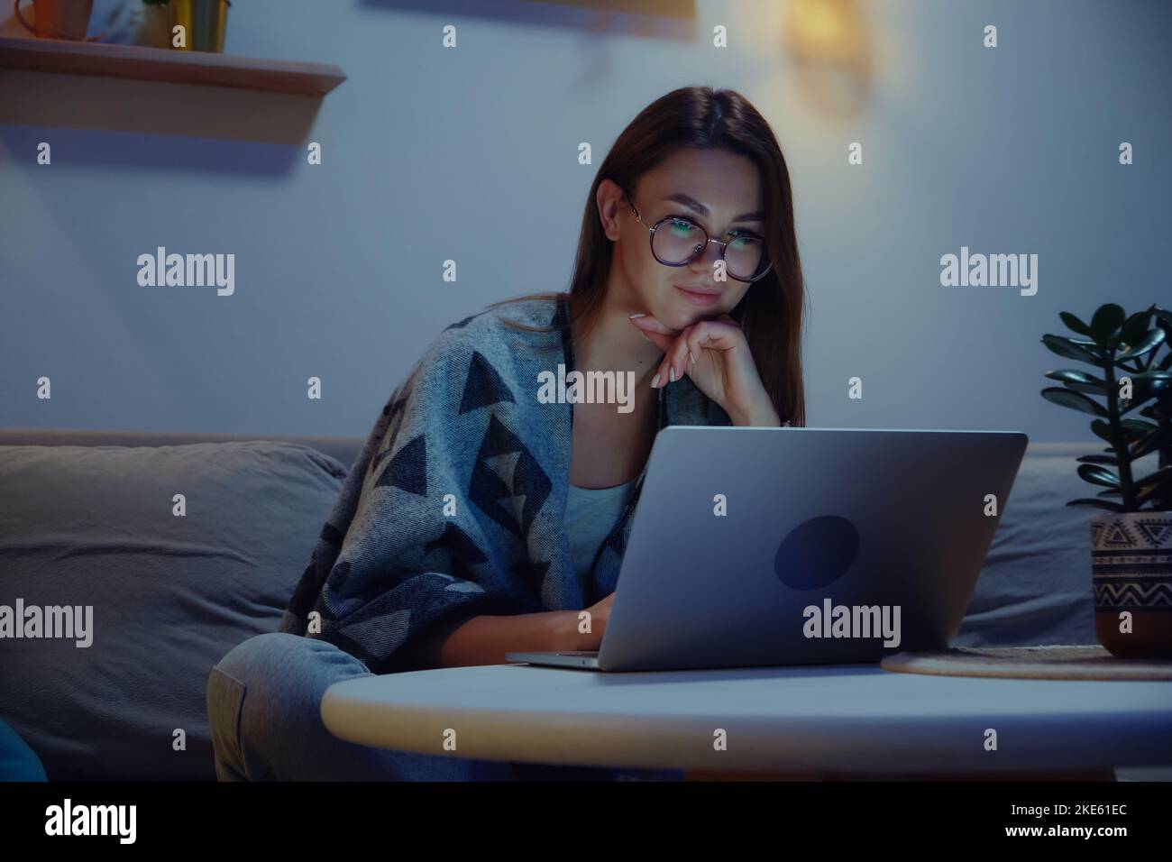 Young smiling woman using laptop at night, working overtime at home ...