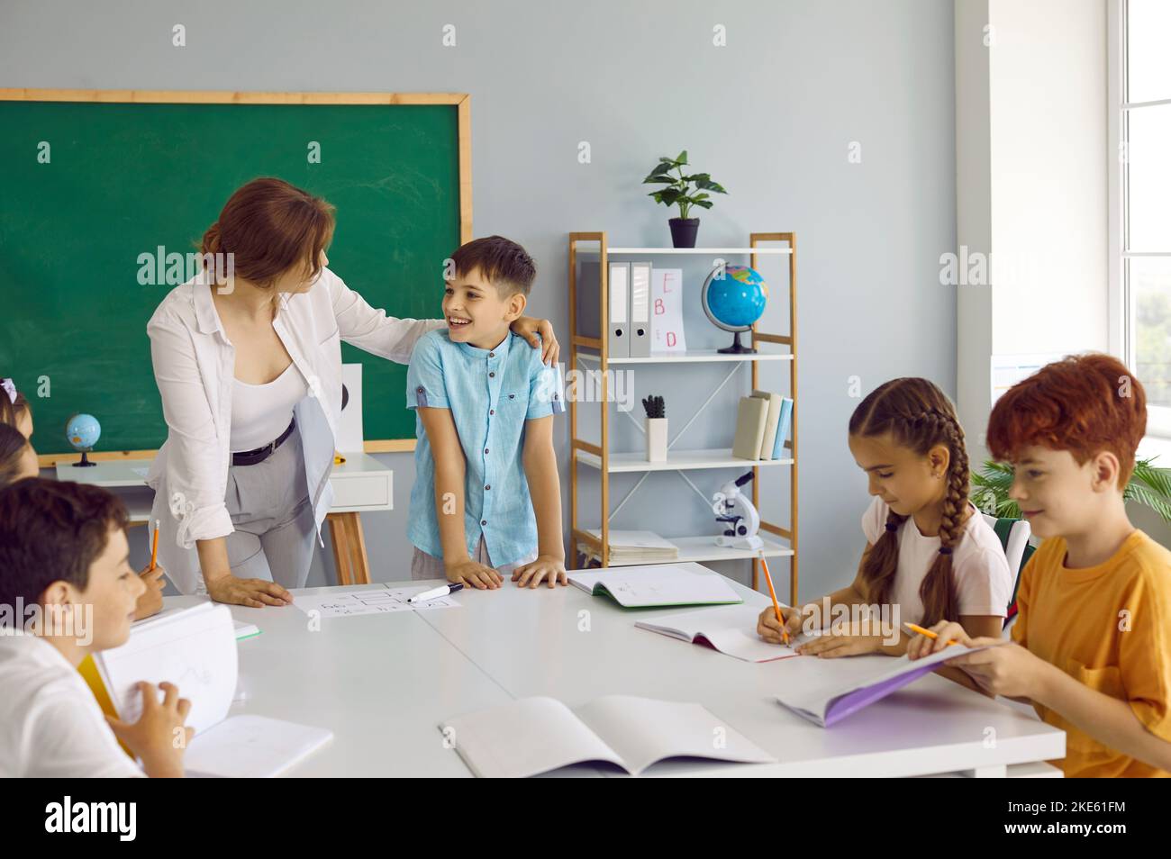 Friendly smiling teacher listens with pleasure to small schoolboy who ...