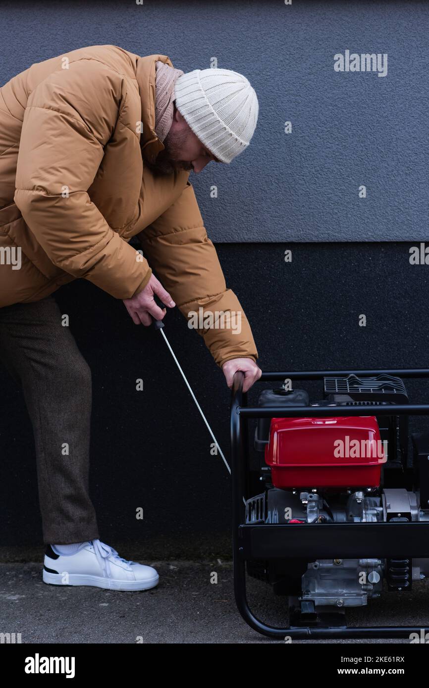side view of man in down jacket and knitted hat starting electricity ...