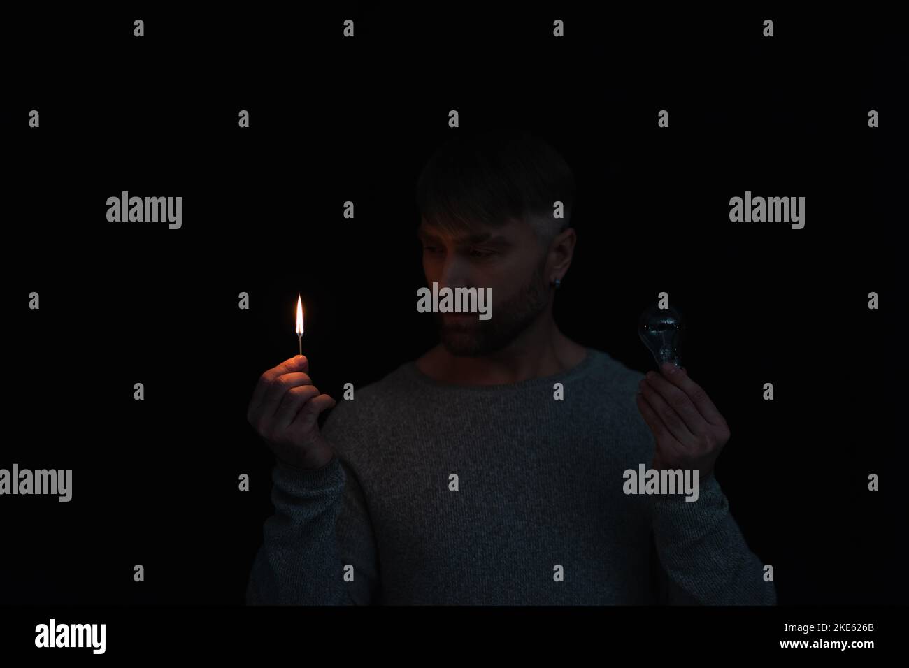 man looking at flame of lit match while holding electric bulb isolated ...