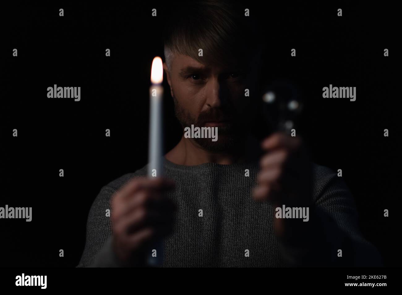 man looking at camera while holding lit candle and light bulb isolated ...