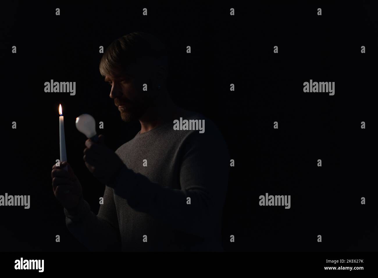 man holding light bulb and burning candle in darkness isolated on black ...