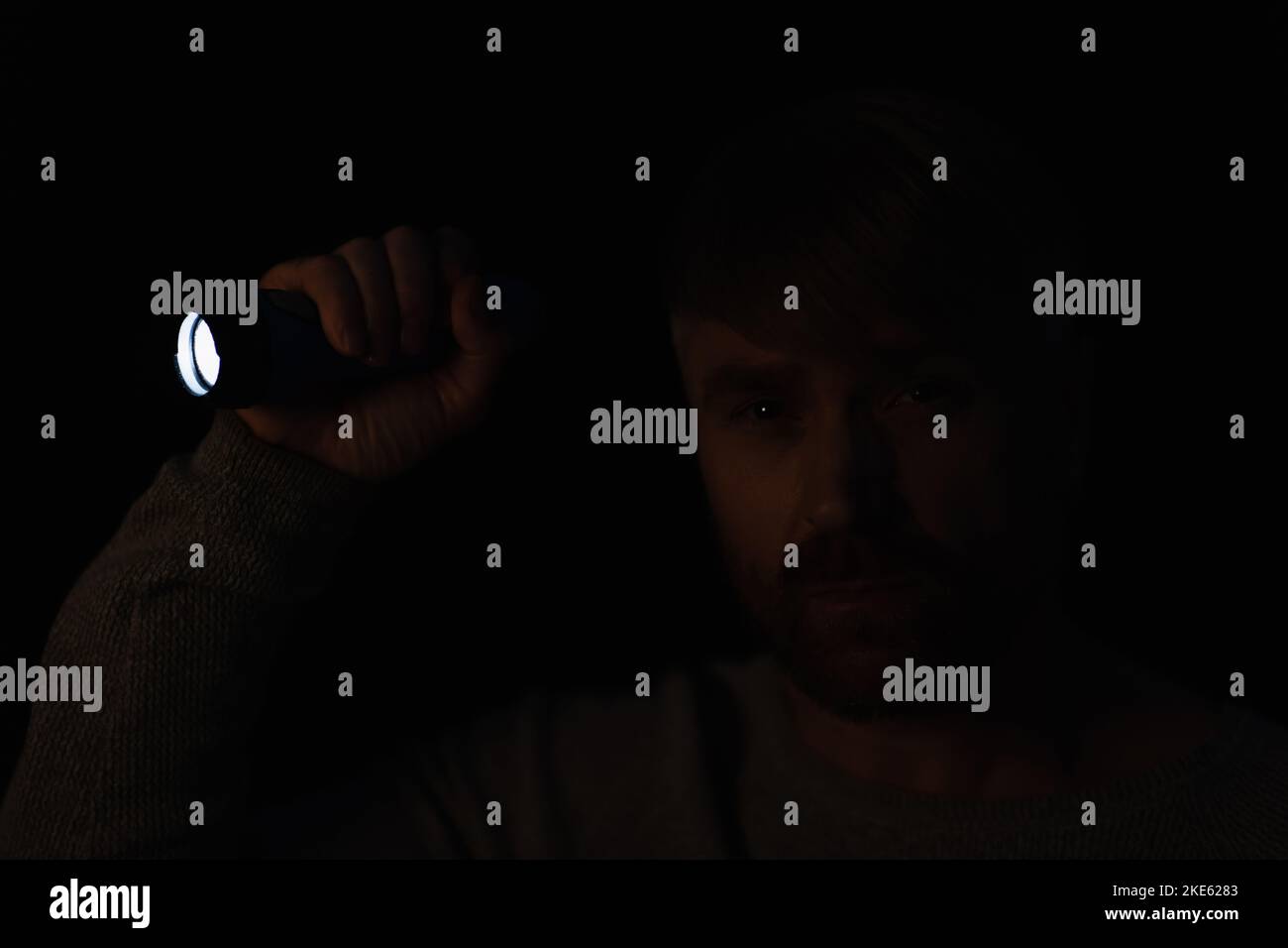 man in darkness looking at camera while holding bright flashlight ...