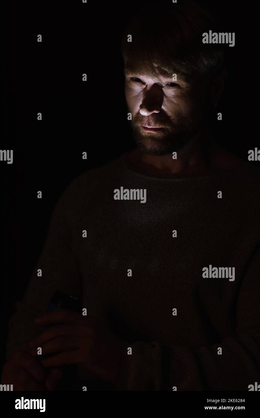 man lighting on face with flashlight while standing in darkness ...