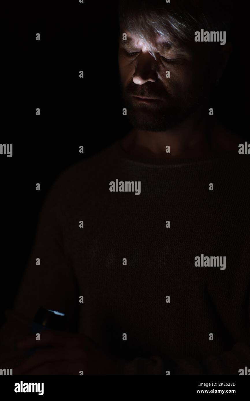 man with glowing flashlight lighting his face during electricity ...