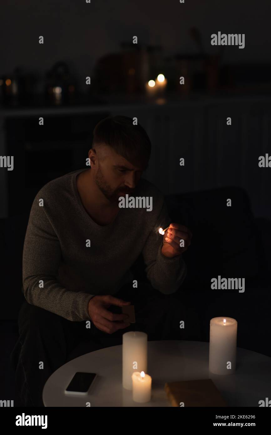 man looking at lit match while sitting in dark kitchen near burning ...