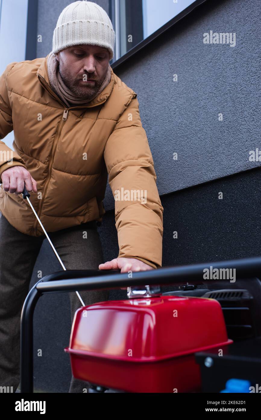 man in warm jacket and hat starting electricity generator during energy ...