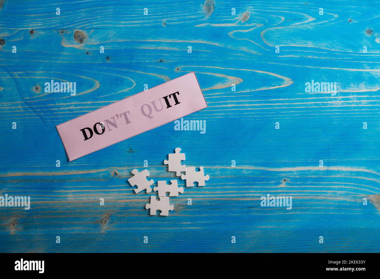 Scattered puzzle pieces placed next to a pink paper with a Dont quit ...