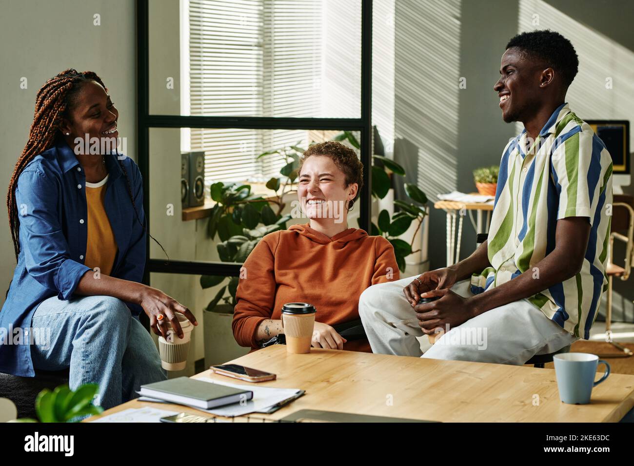 Happy young multicultural colleagues laughing at break while sitting by ...