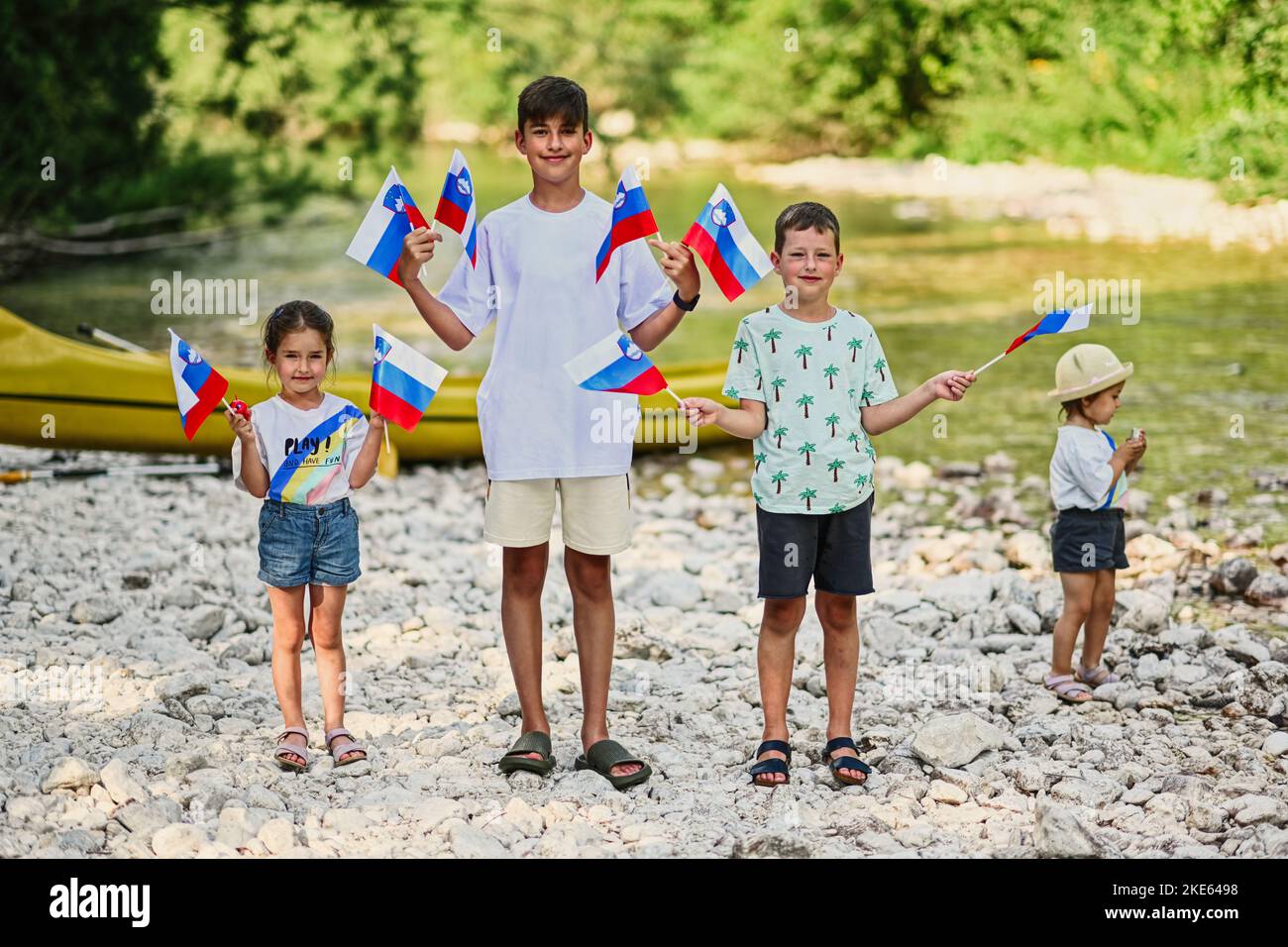 Four kids hold slovenian flags in rocky shore of a calm river in ...