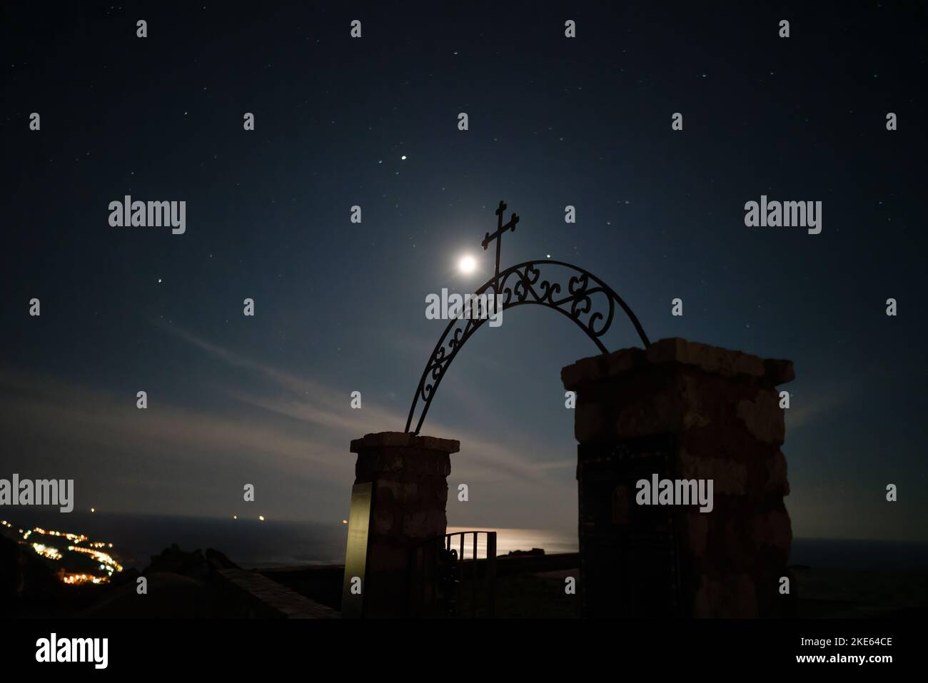A silhouette of a gate entrance with a cross on top in the nighttime ...