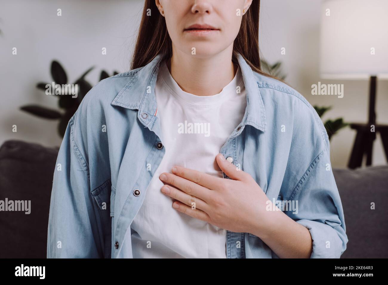 Close-up of upset unhealthy young female sitting on grey sofa at home ...