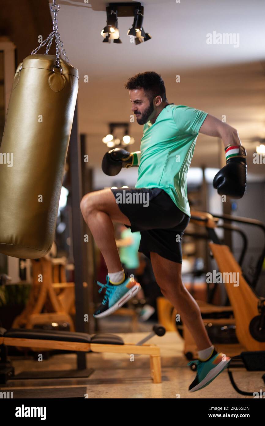 Muscular man with boxing gloves jump hitting a punching bag with a knee ...