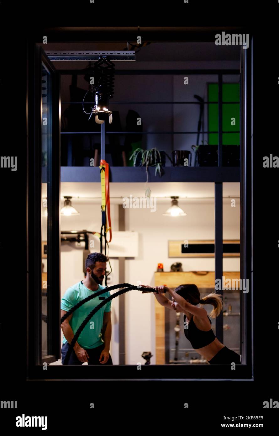Fit girl with exercising with ropes with a male fitness instructor in a ...