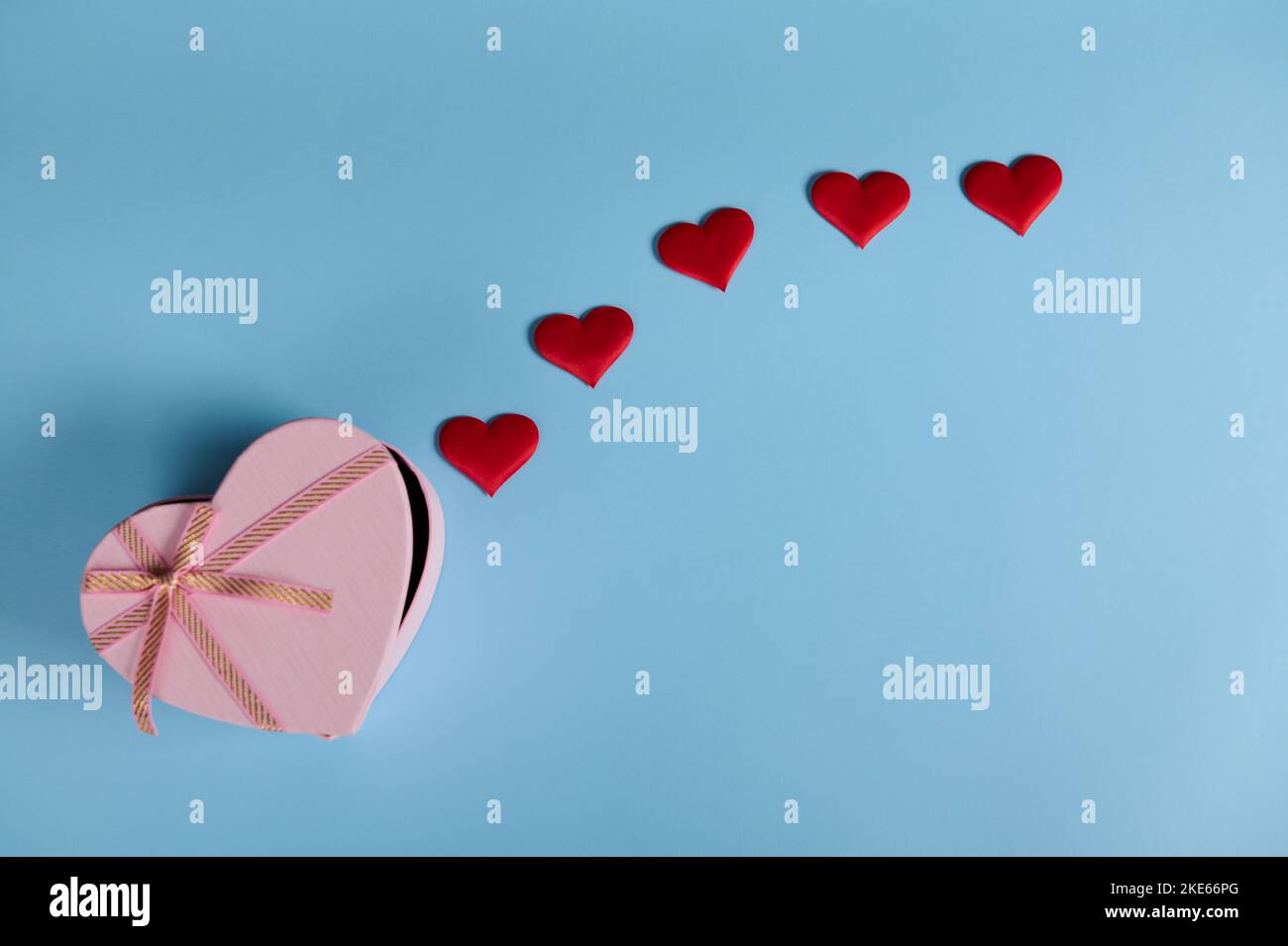 Pink heart shaped gift box and red decorative hearts on pastel blue ...