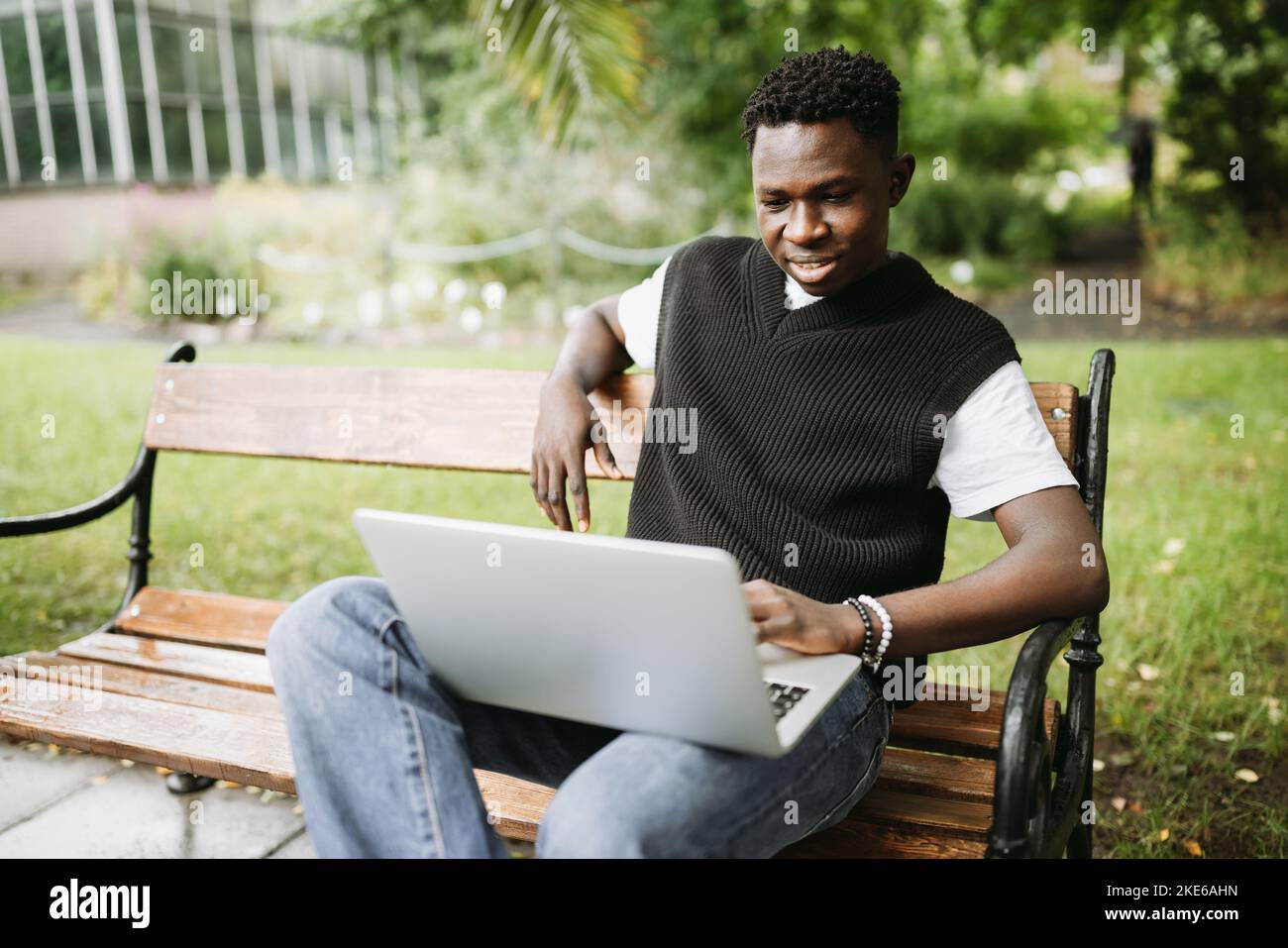 Young black man in vest working on laptop computer outdoors, looking at ...