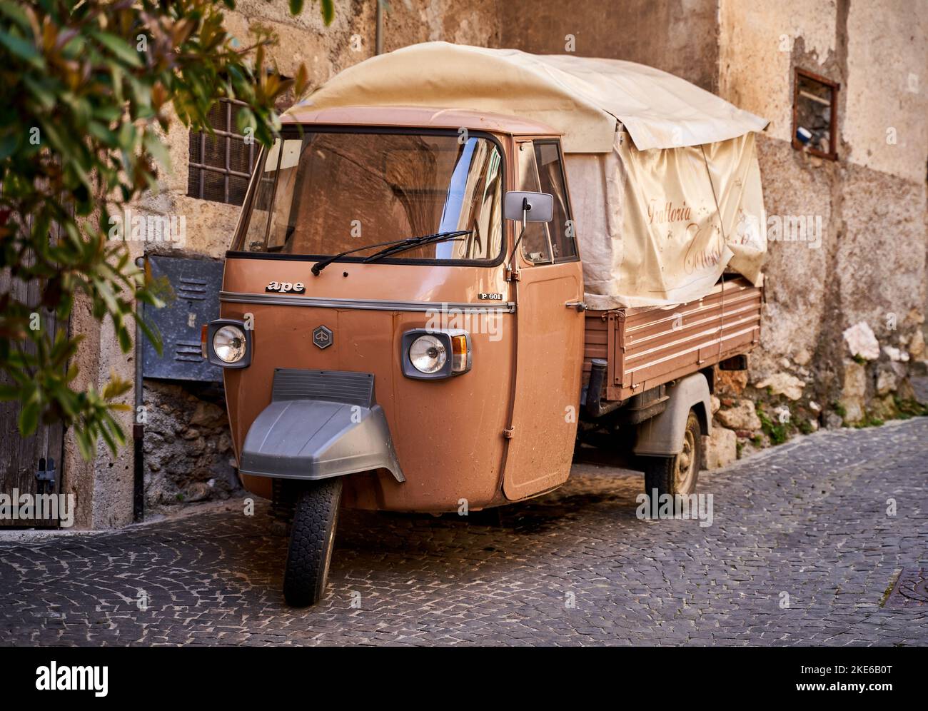 A closeup shot of an old orange Piaggio Ape car on an ancient street ...