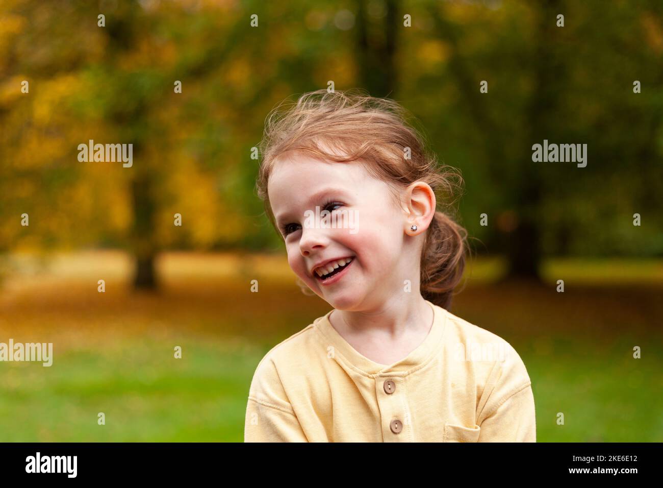 Lovely cute red-haired little girl in the autumn park outdoors. Lovely ...
