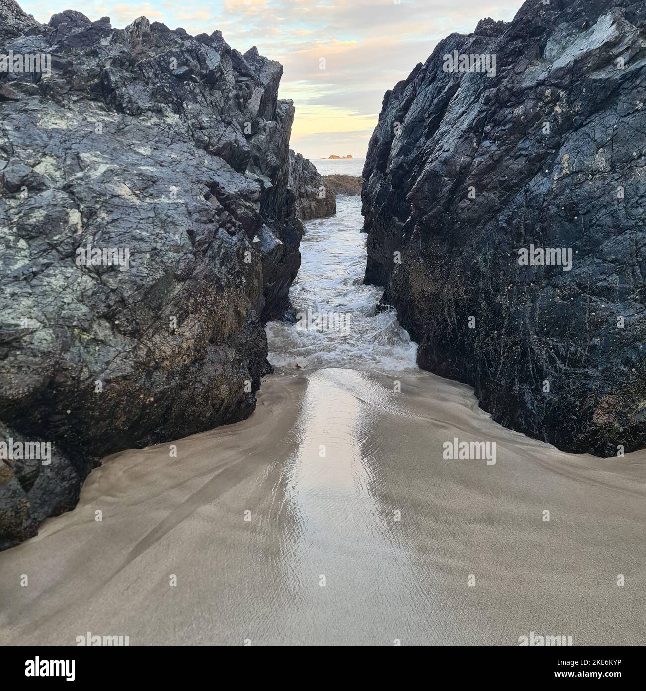 A seascape between huge rocks in a sandy beach at sunset Stock Photo ...