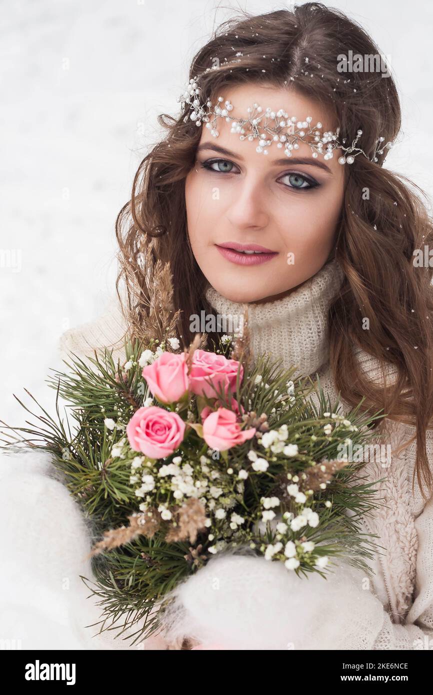 Beautiful bride in a white dress with a bouquet in a snow-covered ...