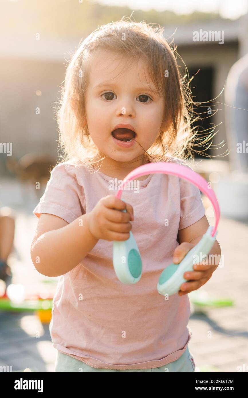 Portrait of a little girl looking at camera putting toy headphones on ...