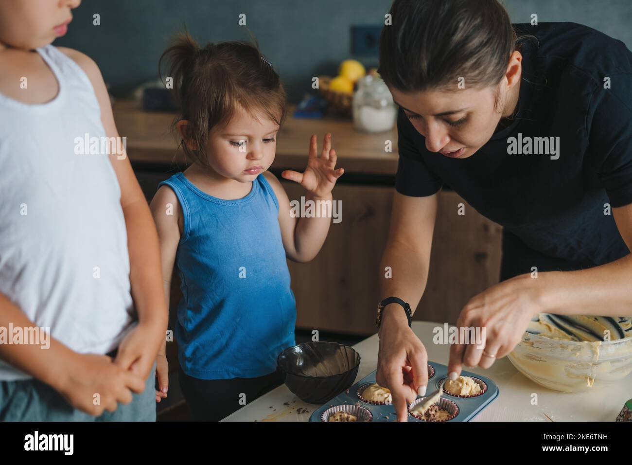 Mother spooning raw dough into baking pans to make birthday cakes ...