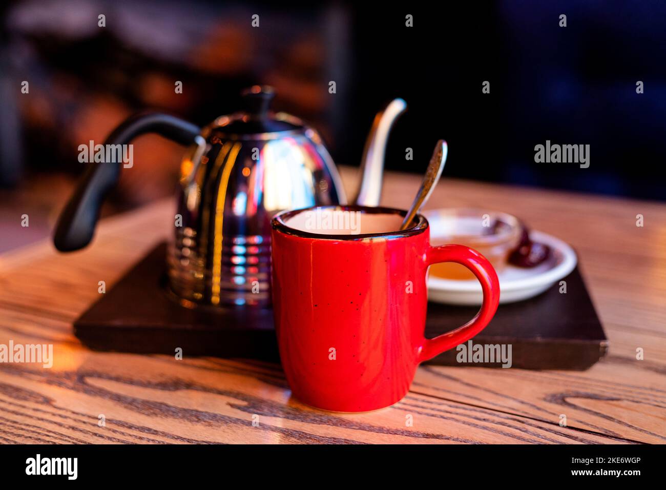 Red cup, metal kettle on a wooden dark table. Tea party in the ...