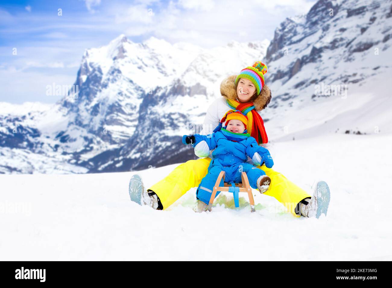 Mother and baby on sleigh ride in the mountains. Child and mom sledding ...