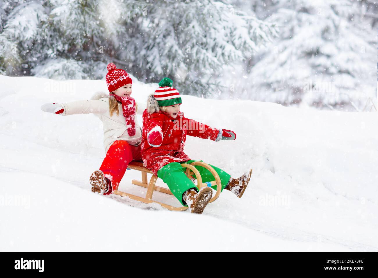 Little girl and boy enjoying sleigh ride. Child sledding. Toddler kid riding a sledge. Children ...