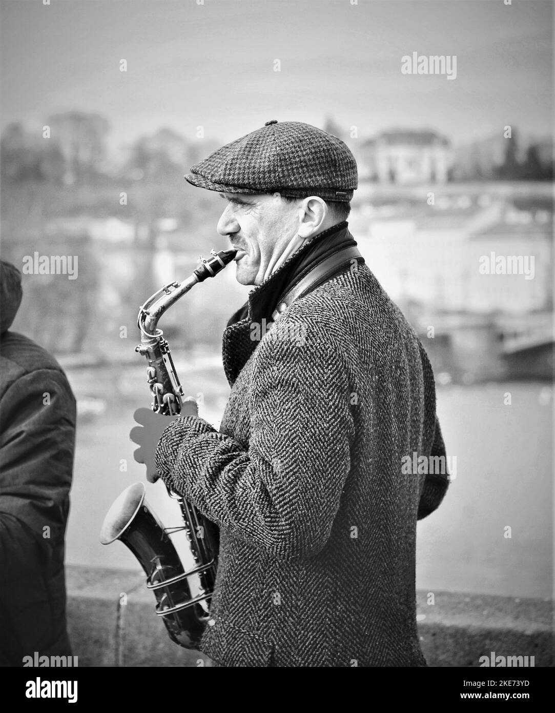 A vertical grayscale of a male playing the saxophone outdoors, pond and ...