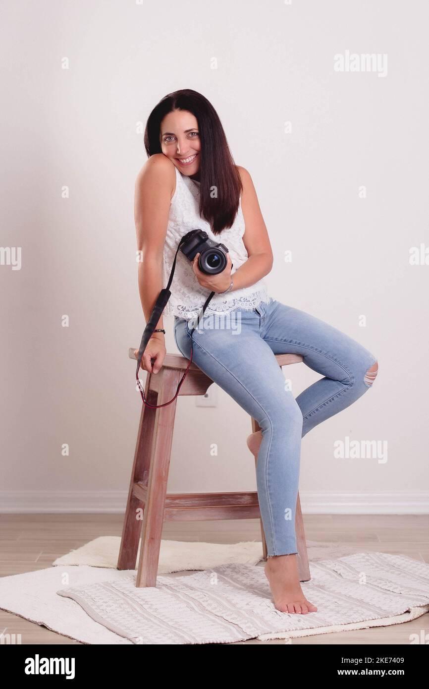 A vertical of a female holding a canon camera while sitting on the ...