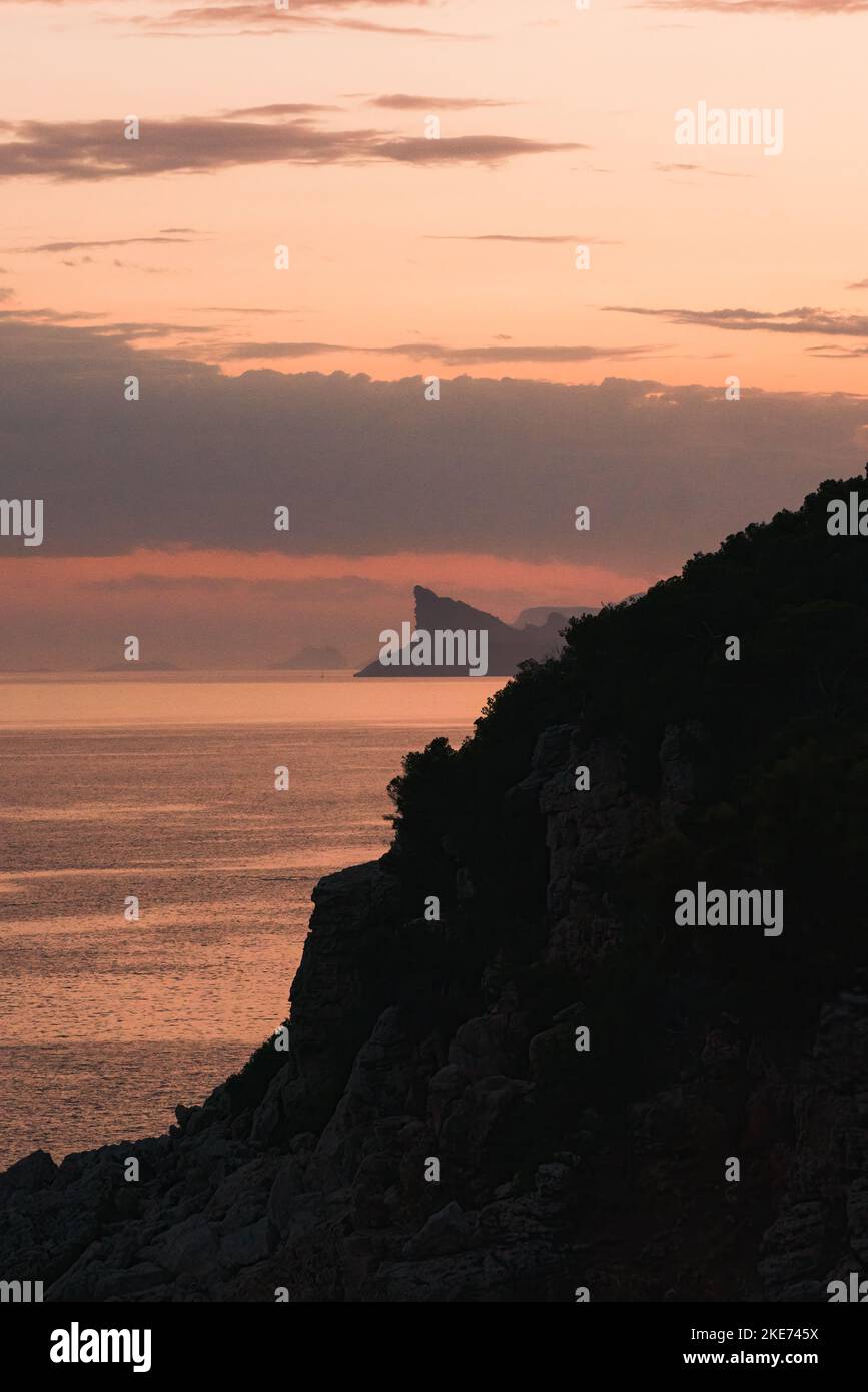 A vertical of sunset over the sea with a forested hill silhouette ...