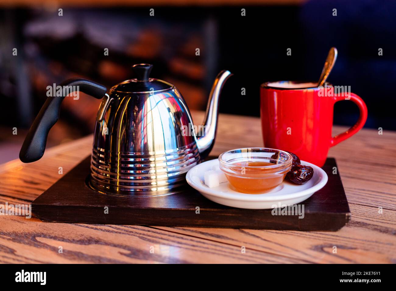 Red cup, metal kettle on a wooden dark table. Tea party in the ...