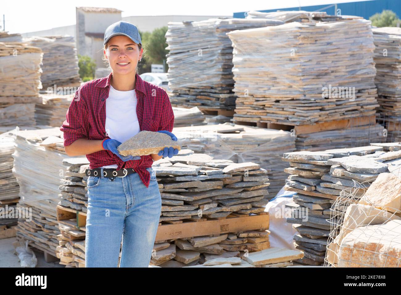 Young positive manager girl demonstrates a stone tile in a warehouse ...