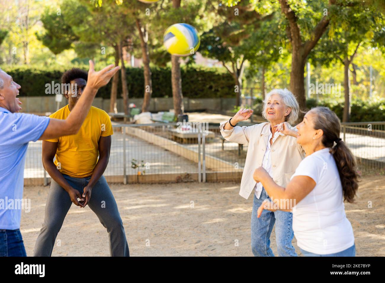 Joyful multiracial group of mature adult people playing volleyball game ...