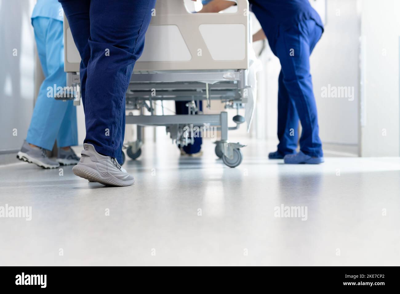 Low section of healthcare workers pushing patient in bed down hospital ...