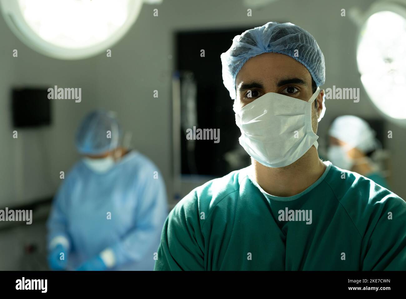 Portrait of biracial male surgeon in surgical cap and mask in operating ...