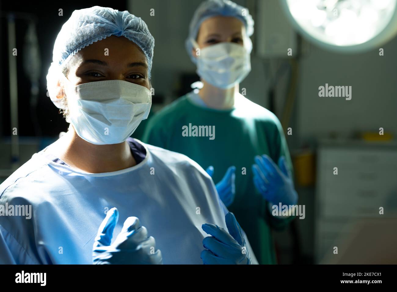 Portrait of smiling biracial female surgeon in cap and mask in ...