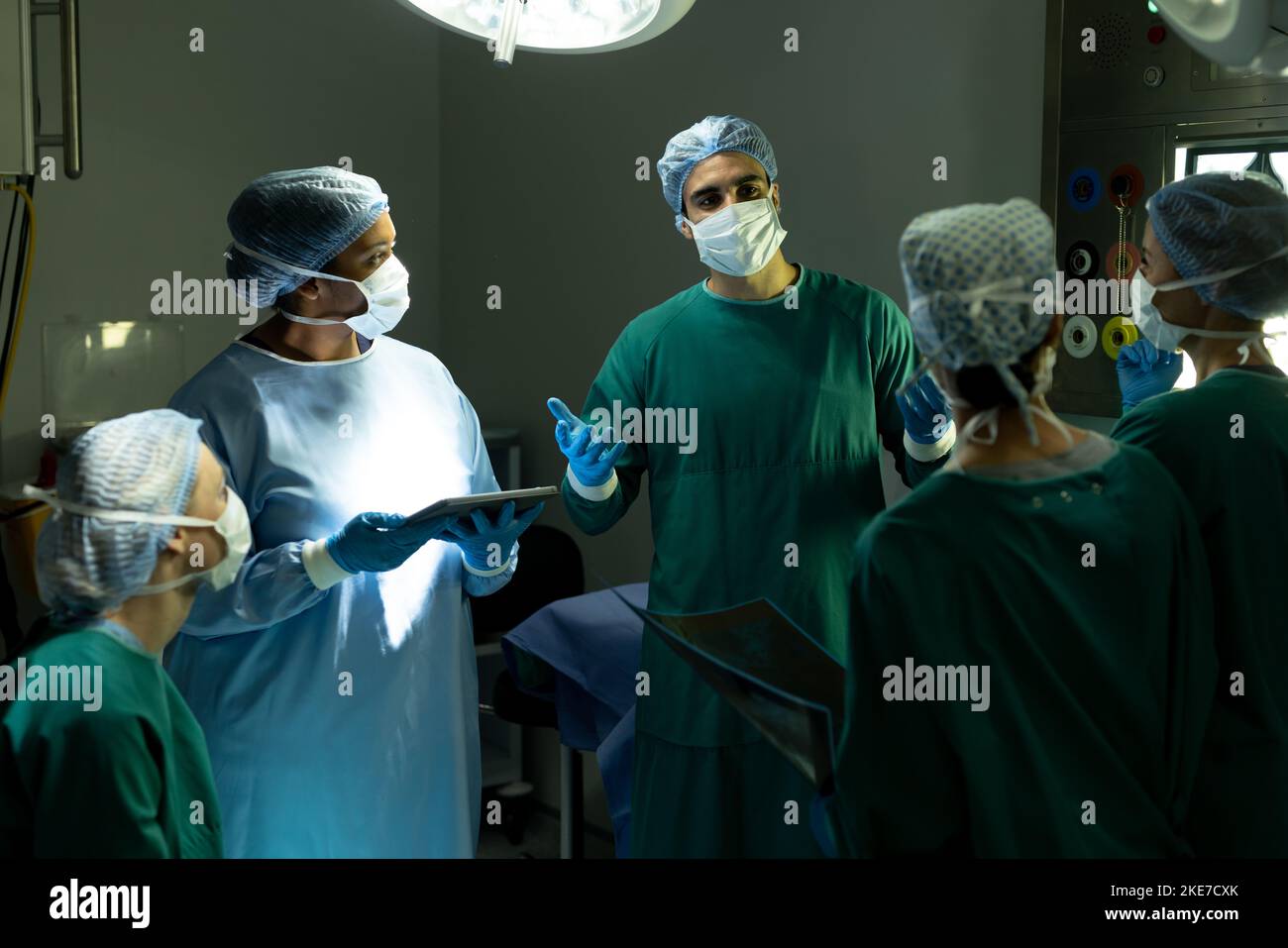 Diverse group of surgeons in discussion, using tablet in operating ...