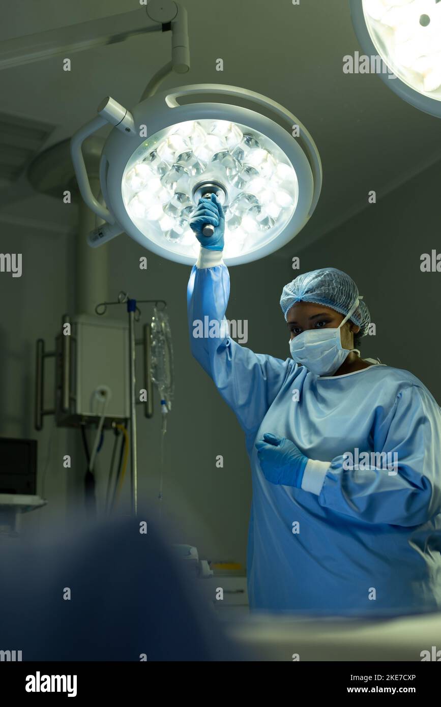 Vertical of biracial female surgical tech adjusting light in operating ...