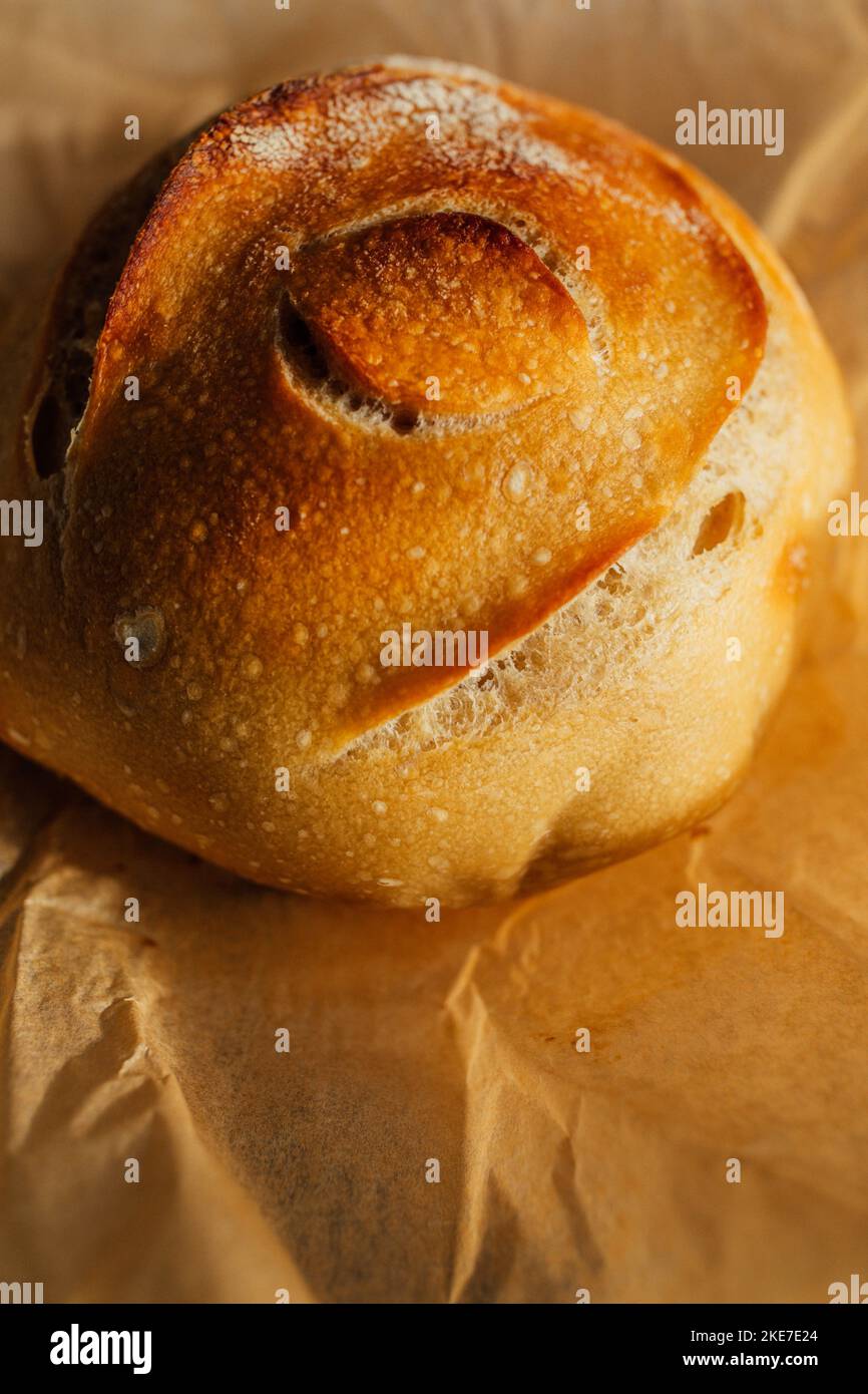 Freshly baked round loaf of homemade sourdough bread on brown parchment ...