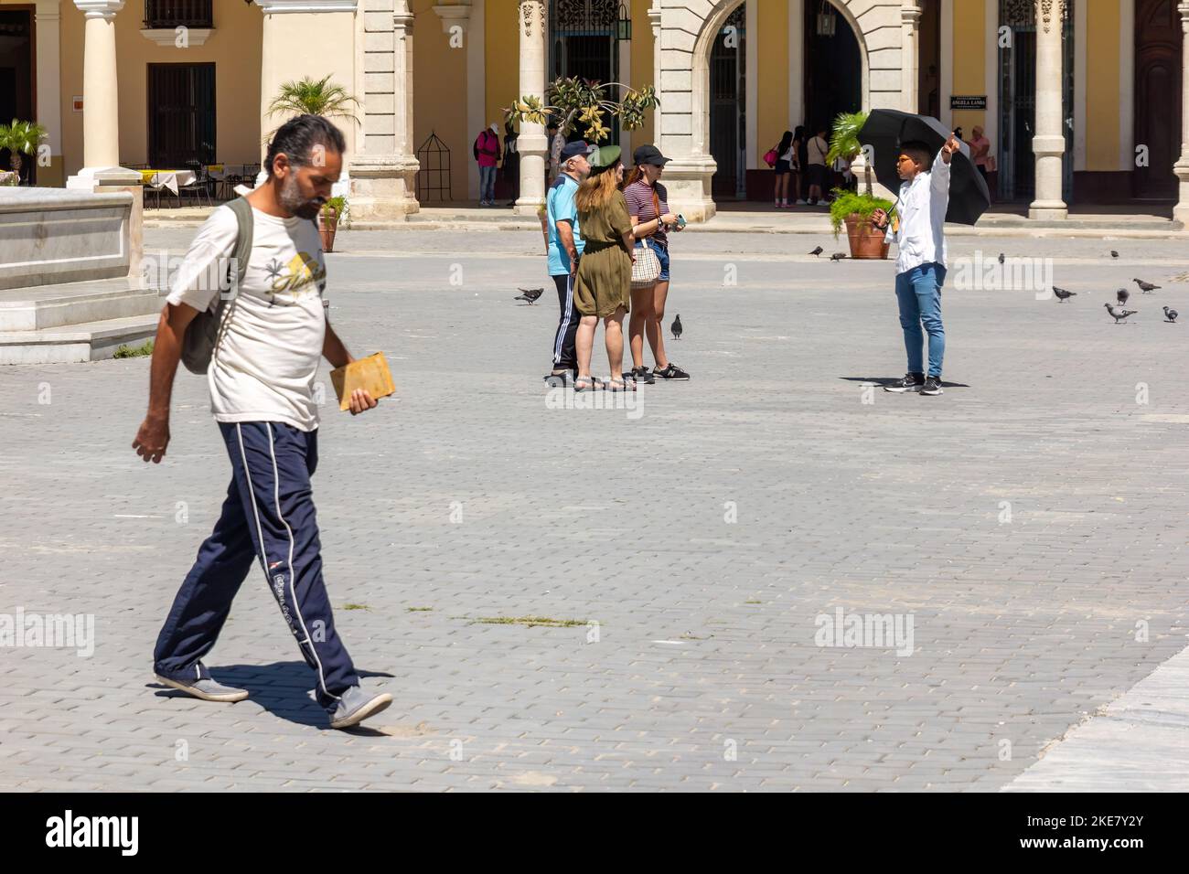 Cuban man walking in Old Havana. A group of foreign tourists interacts ...