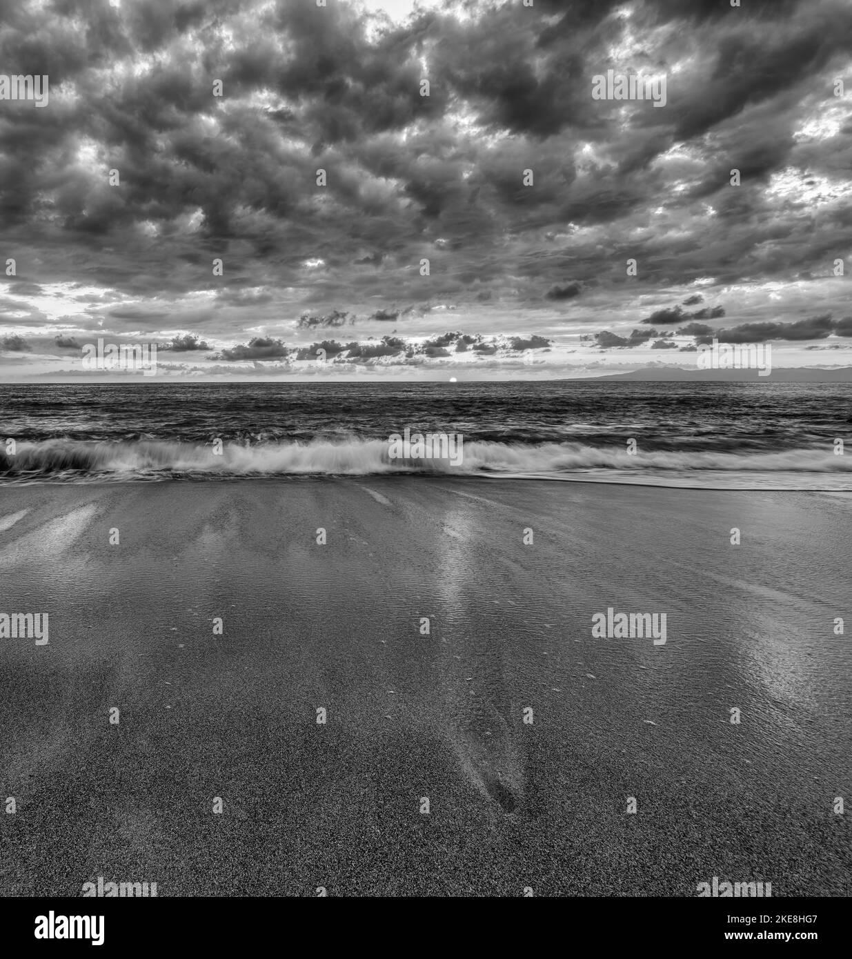 A grayscale shot of a wavy ocean with a cloudy sky in the background ...