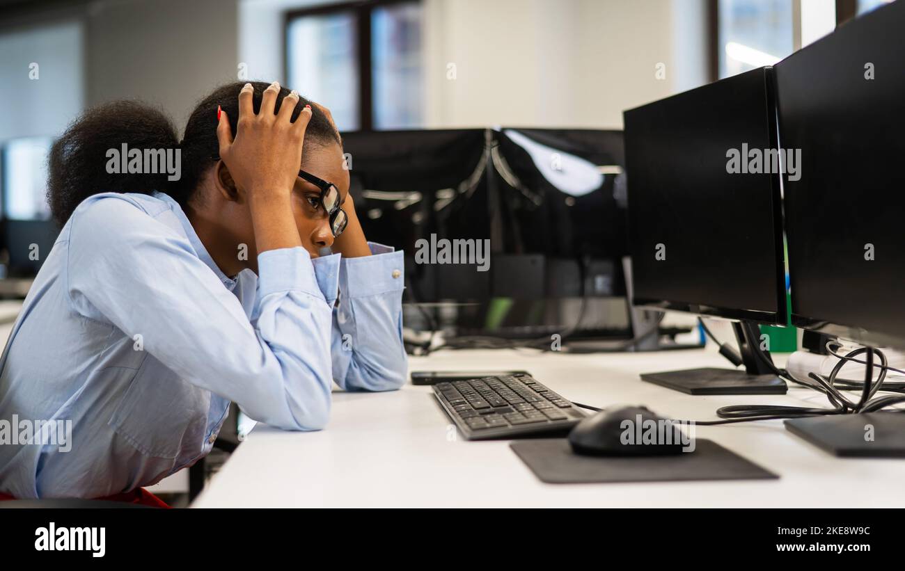 African young woman sitting at her desk clutching her head Stock Photo ...