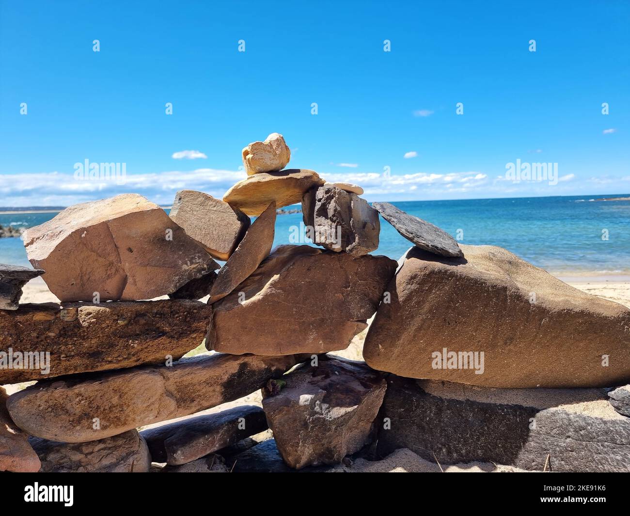 A rock stacking on the sandy beach shore with blue water in Swansea ...